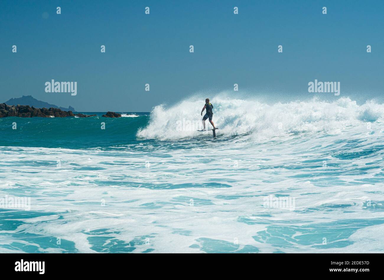 A man surfs on a hydrofoil surfboard on turquoise waves at Mangawhai ...