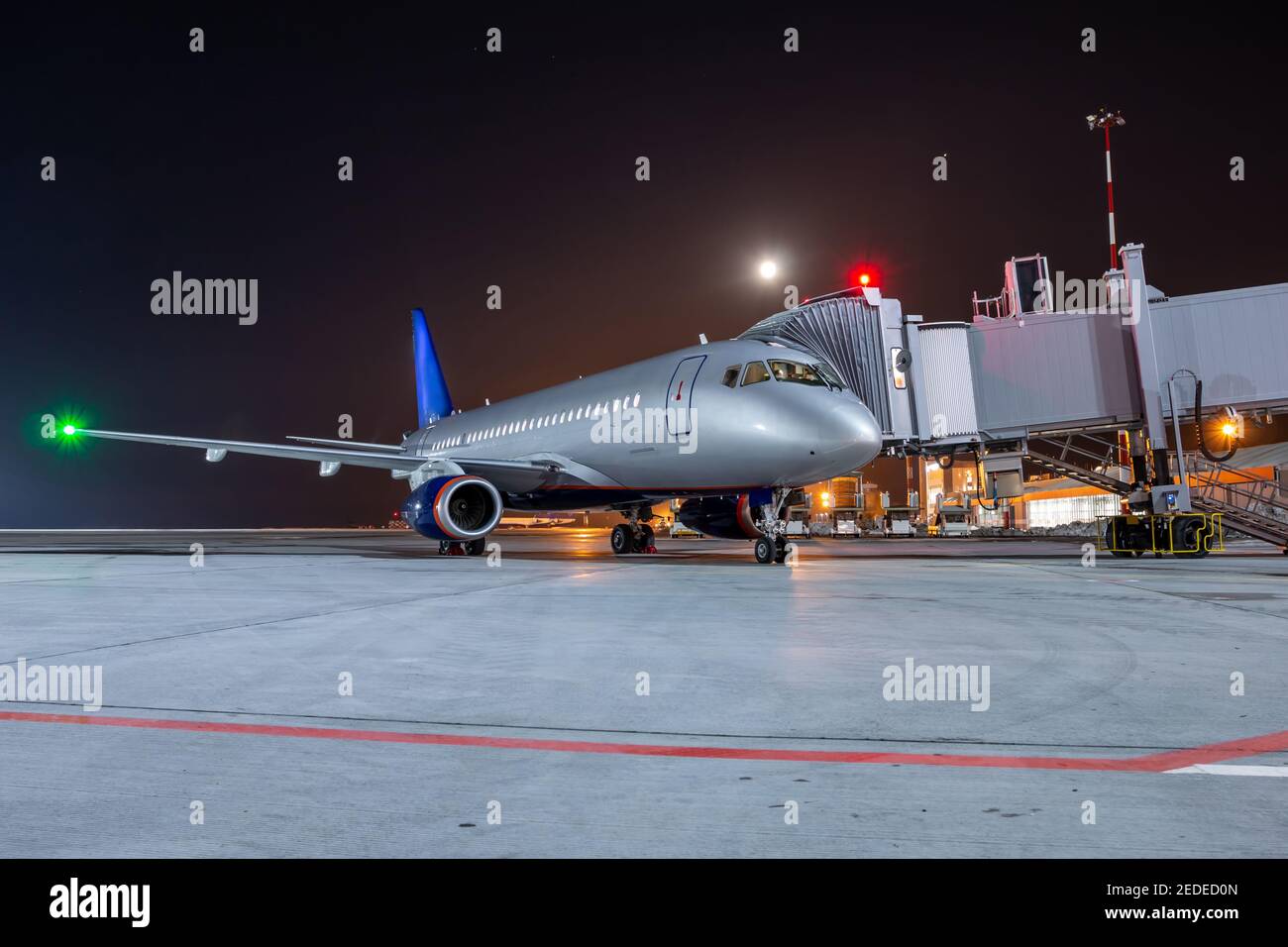 Modern passenger airliner at the jet bridge on night airport apron ...