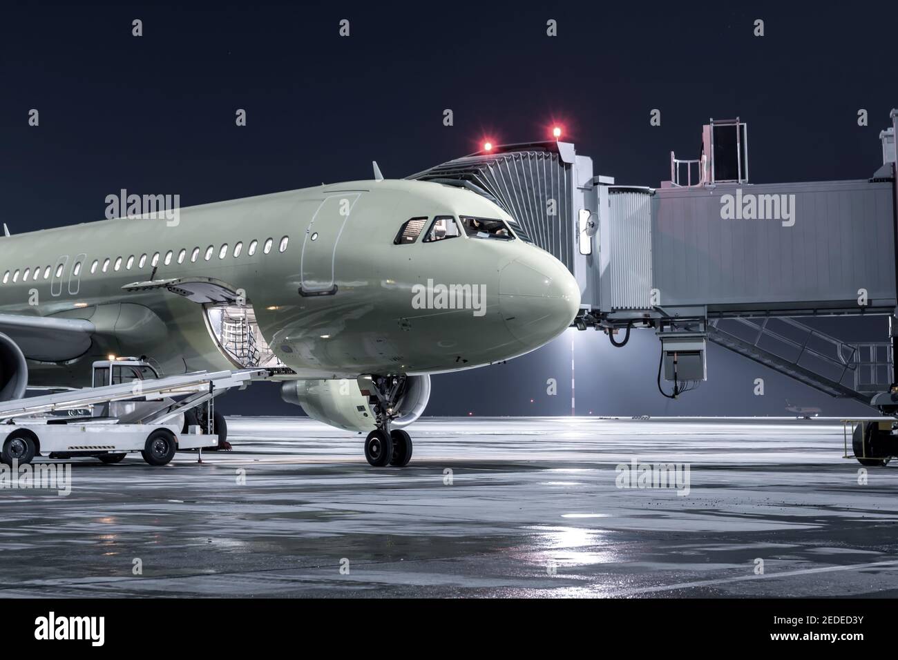 The passenger airplane stands at the jetway on an airport night apron ...