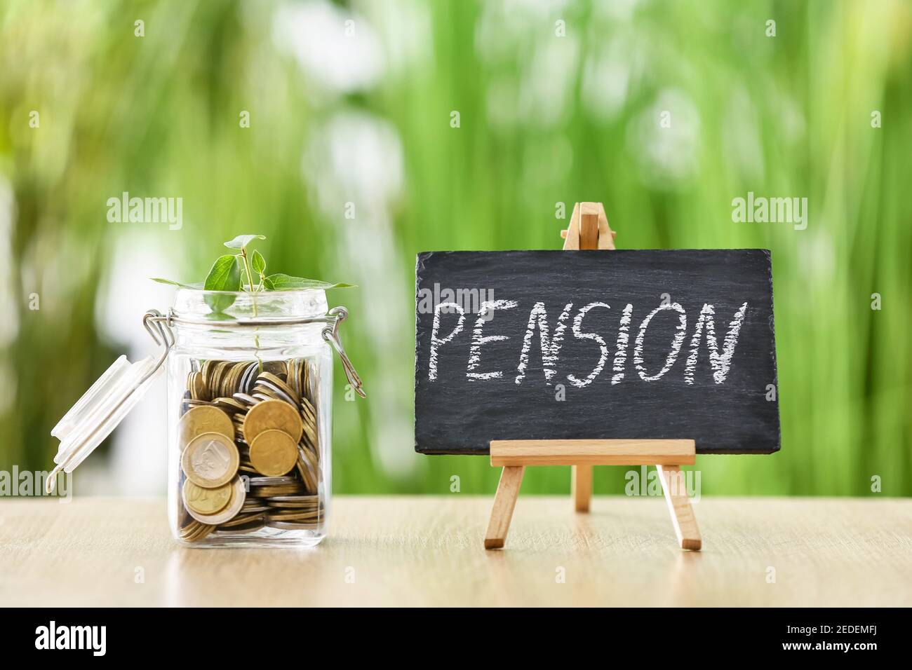 Jar with savings, young plant and chalkboard with word PENSION on table ...