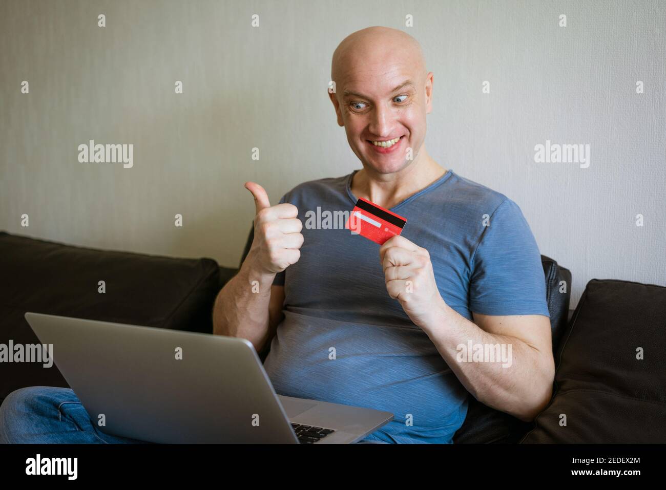 Emotional bald man on the couch with a laptop and credit card in his ...