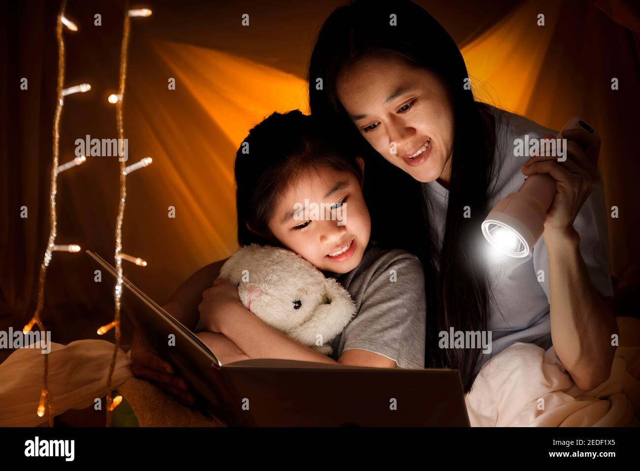 Family concept. elder sister and sister reading book with flashlight ...