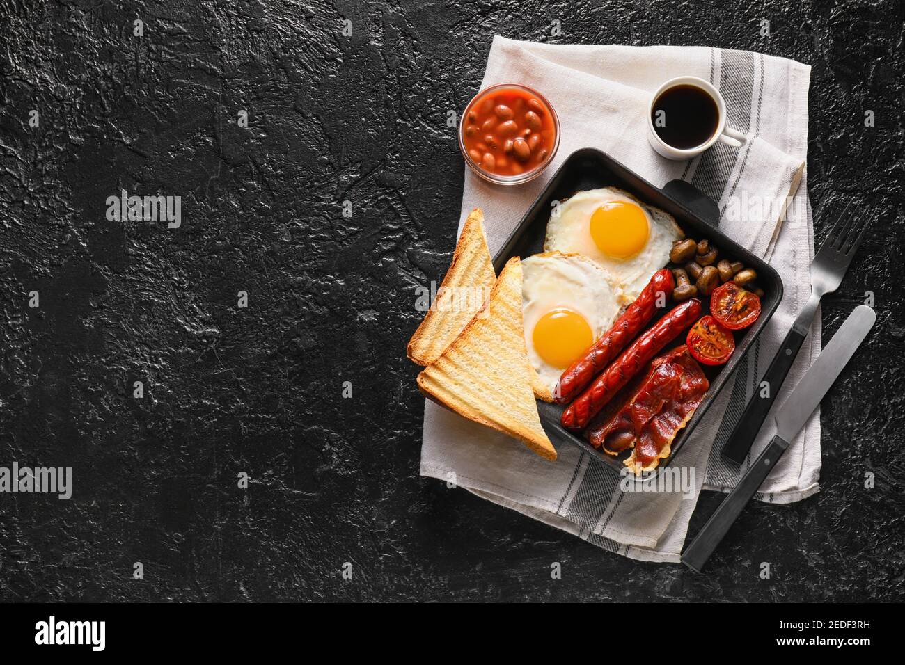 Traditional English breakfast with fried eggs in pan on dark background ...