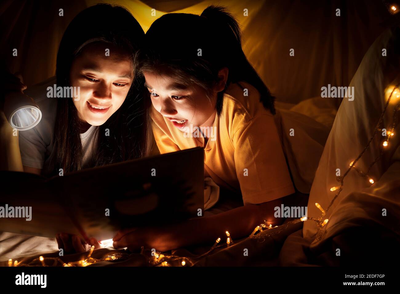 Family concept. Mother and child daughter reading book with flashlight ...