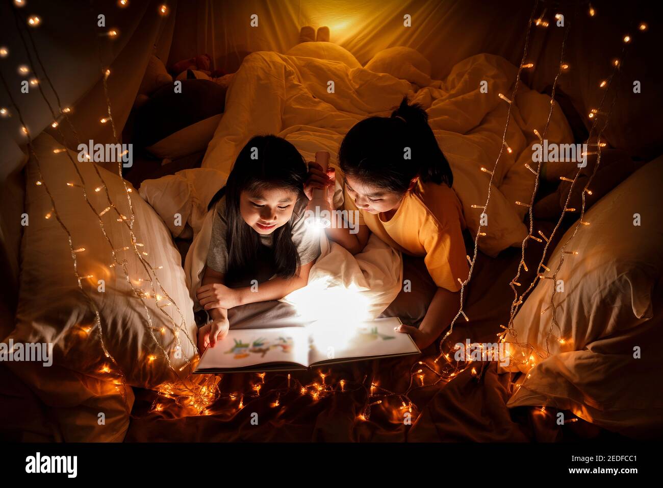 Family concept. elder sister and sister reading book with flashlight ...