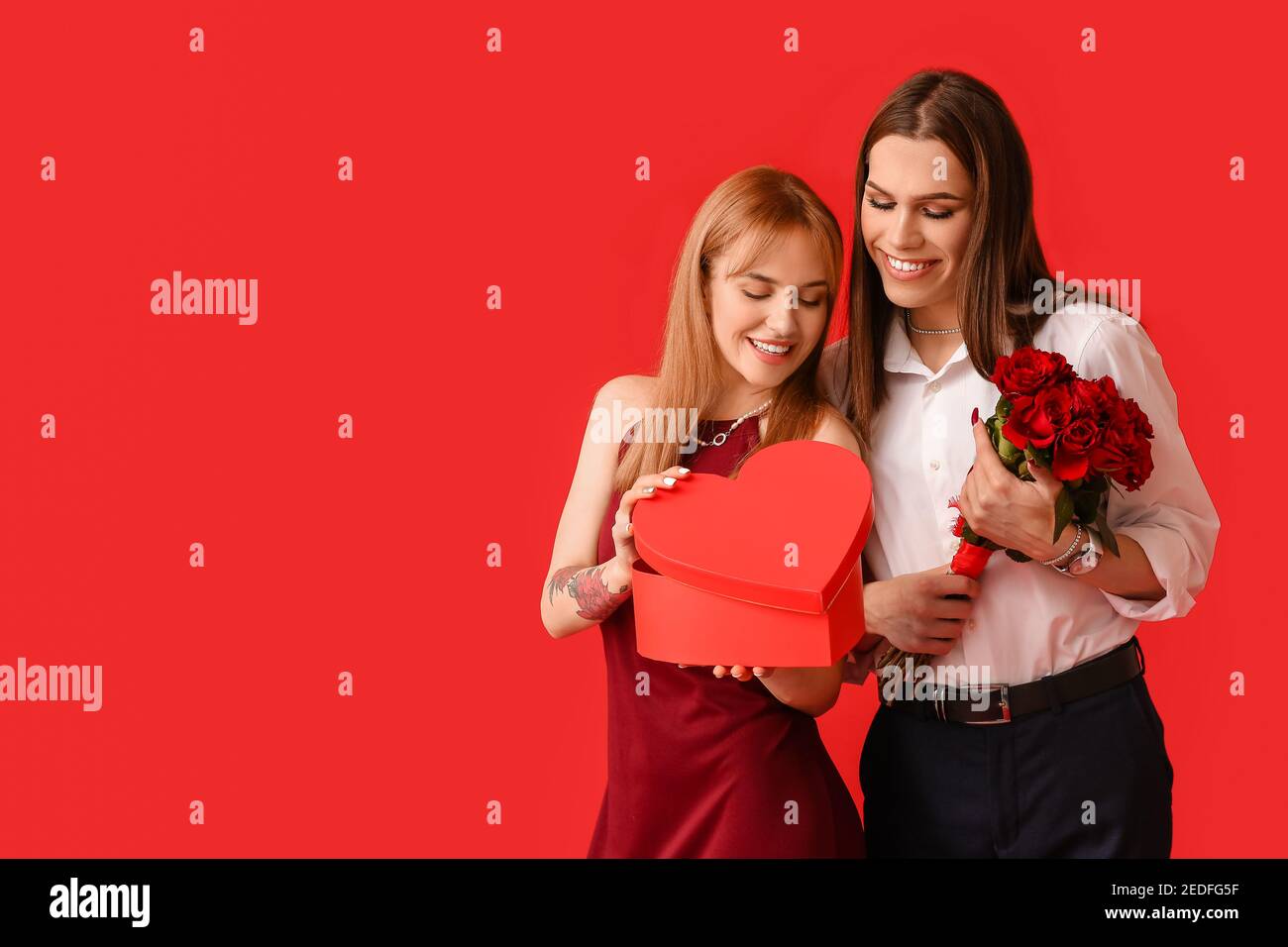 Young transgender couple with flowers and gift on color background ...