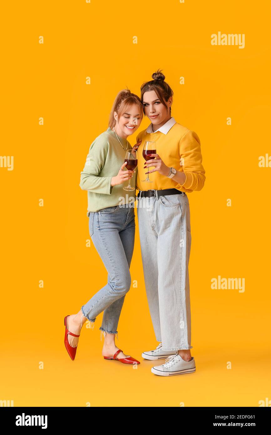 Young transgender couple with glasses of wine on color background ...