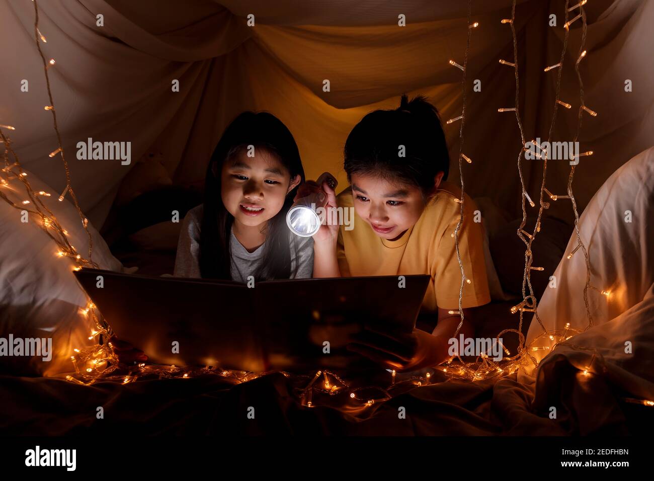Family concept. elder sister and sister reading book with flashlight ...