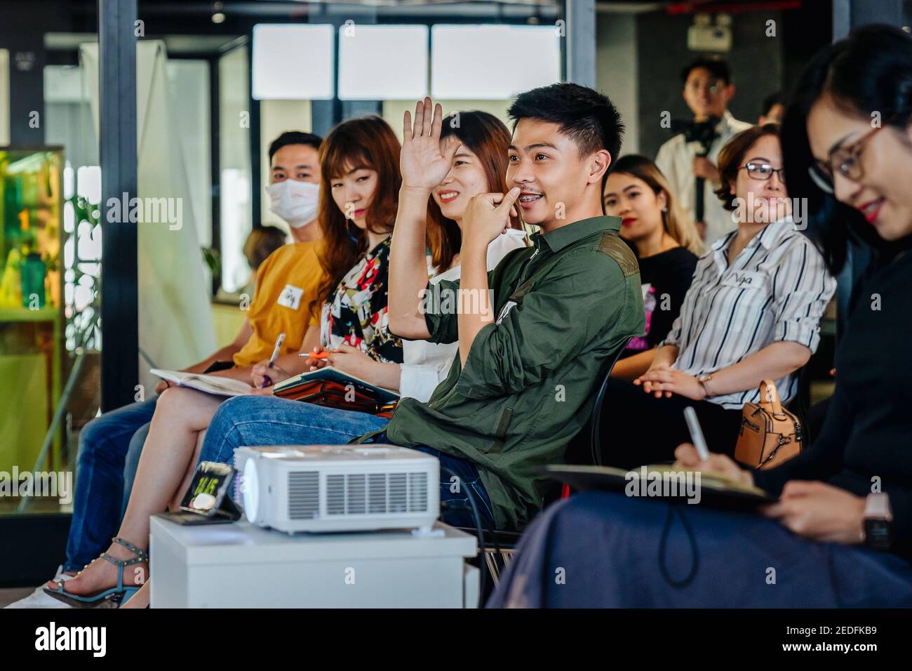 Young man raising hand in audience full of people Stock Photo - Alamy