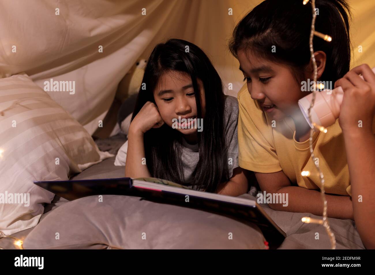 Family concept. elder sister and sister reading book with flashlight ...