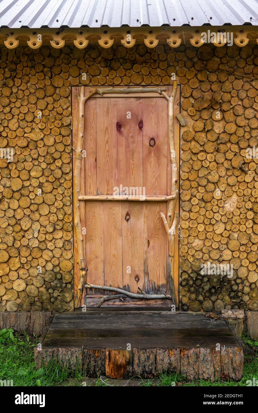 Wooden door on the background of the wall covered with pieces of logs ...