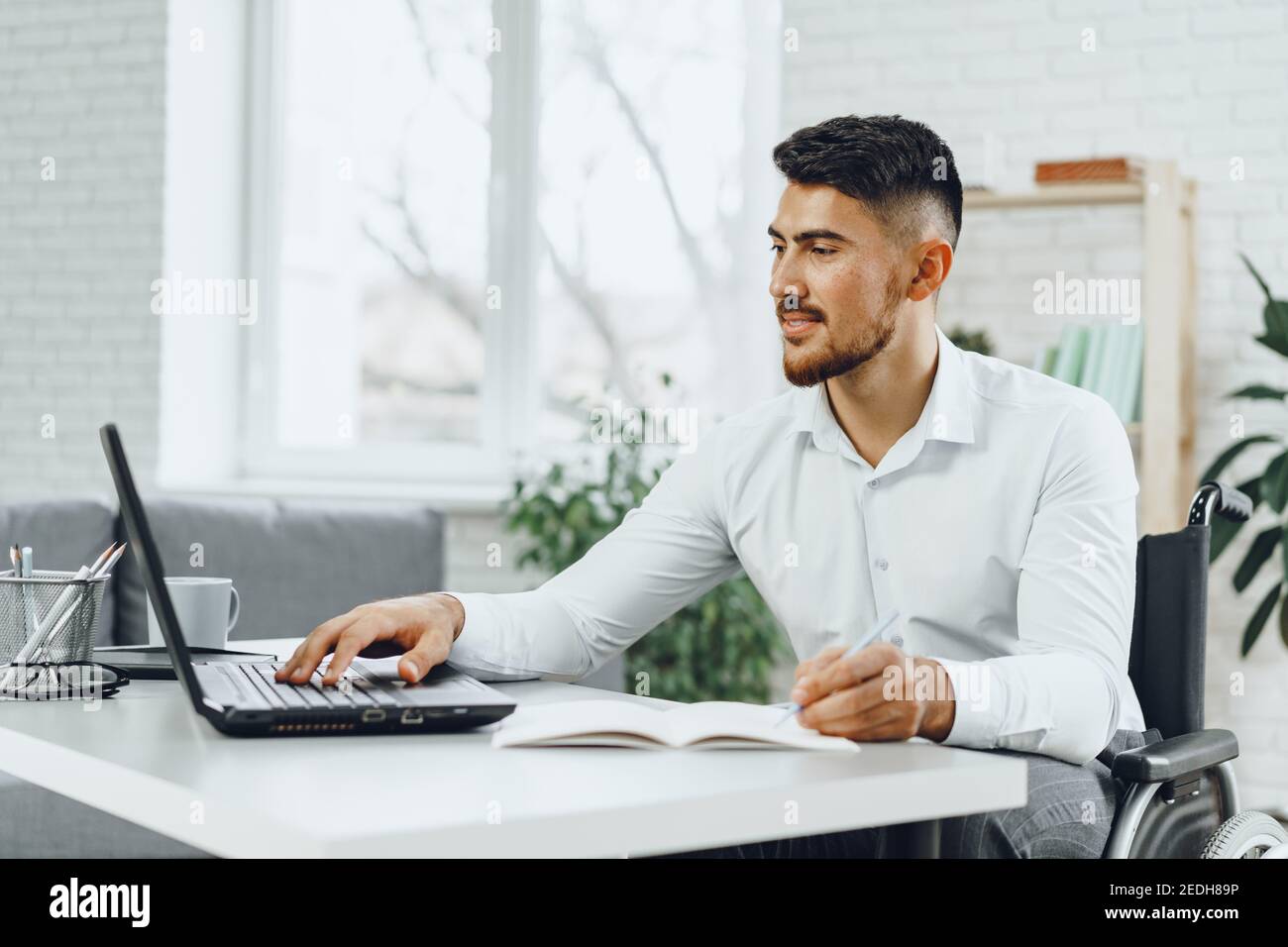 Positive disabled young man in wheelchair working in office Stock Photo ...