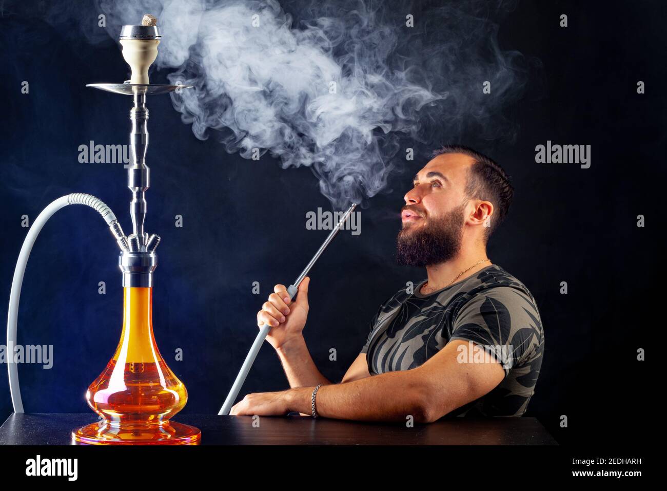 Bearded young man smoking shisha in a dark night club Stock Photo - Alamy