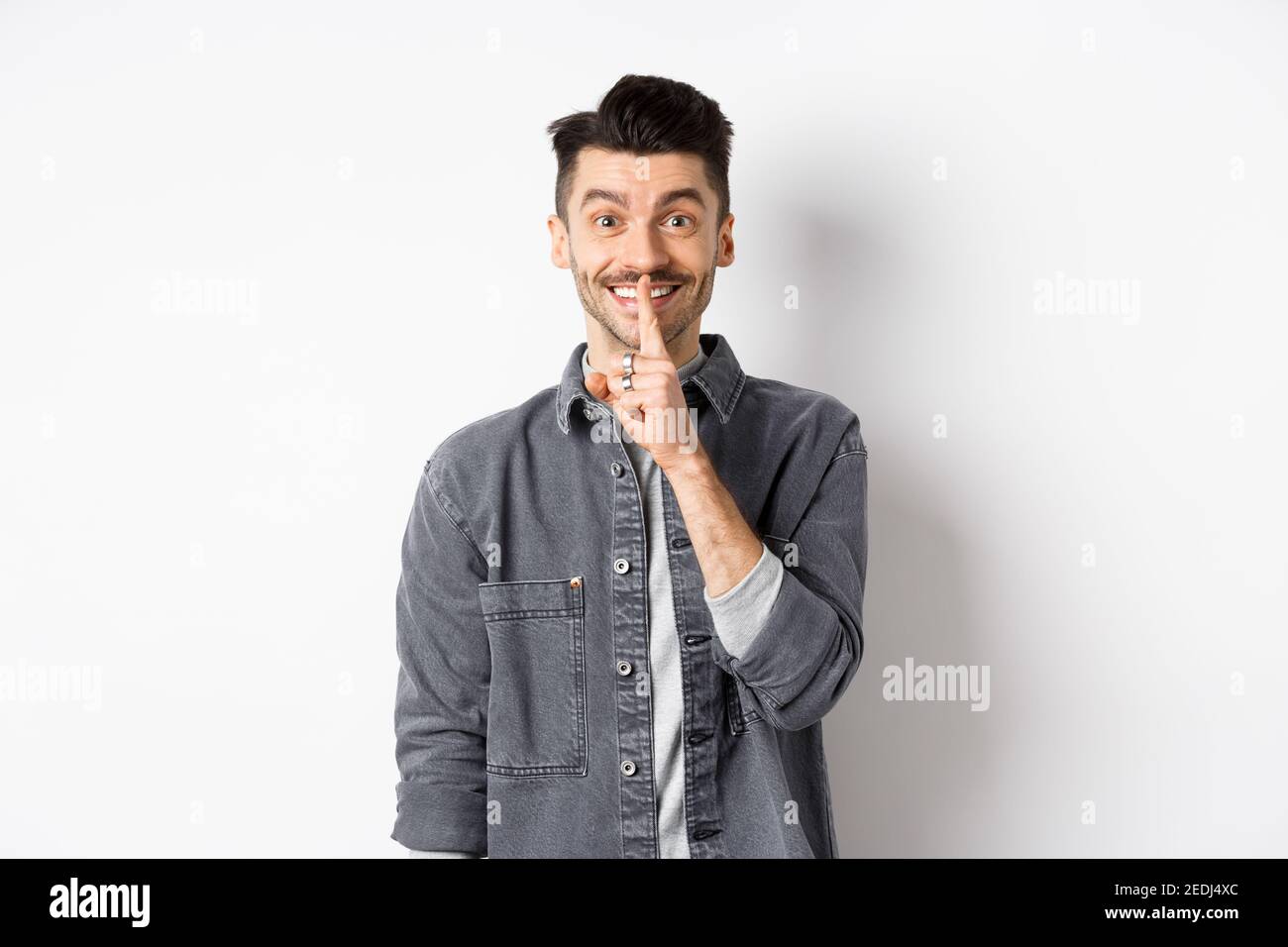 Happy guy shushing at camera, smiling with finger on lips, asking to ...