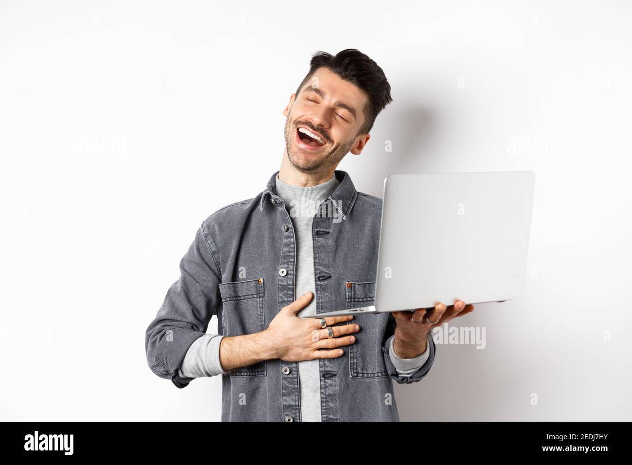 Image of happy guy laughing at funny video on laptop, touching belly ...