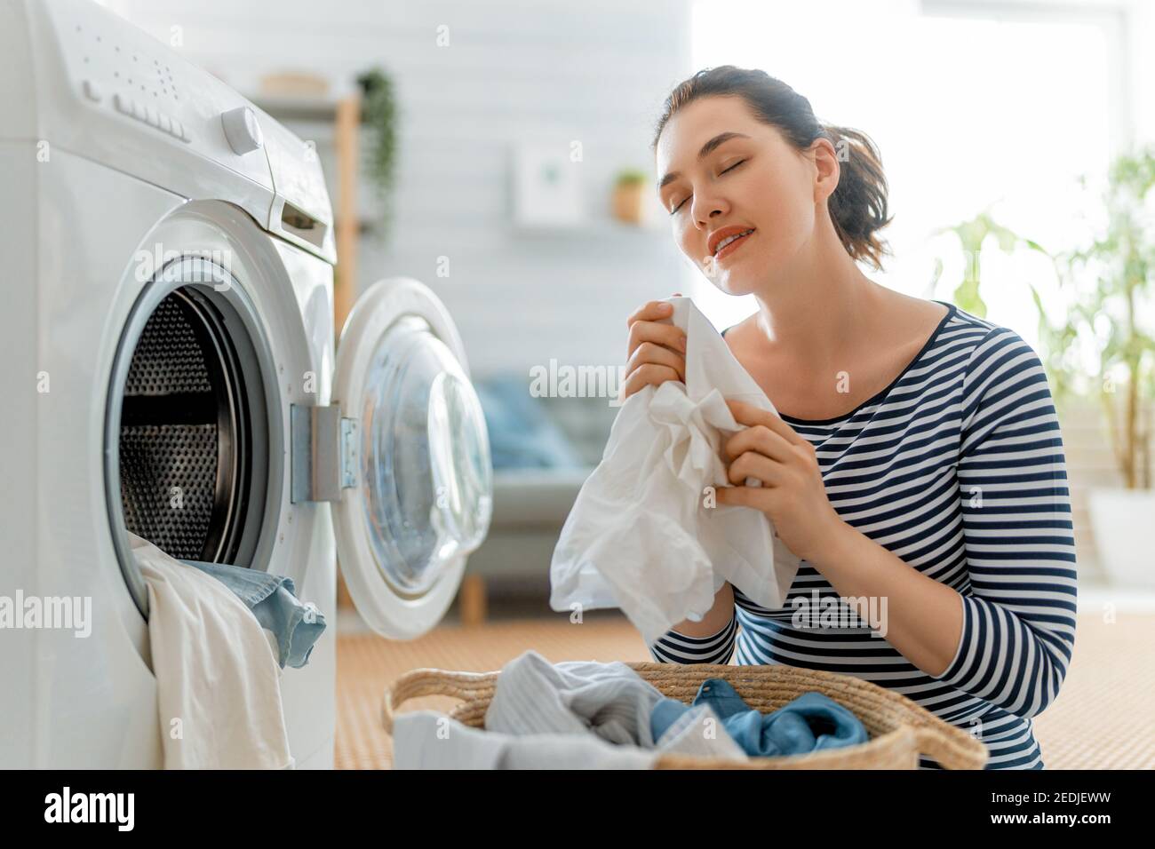 Beautiful young woman is smiling while doing laundry at home Stock Photo - Alamy
