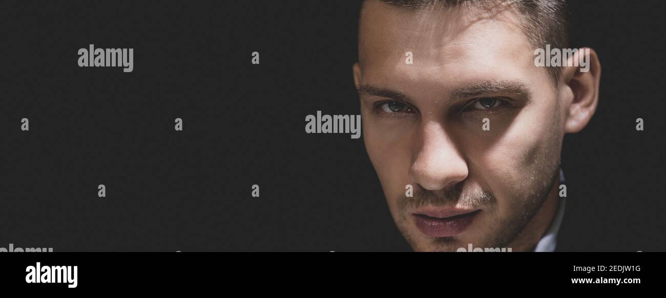 Face of tricky sly man staring at the camera in dark shadow banner ...