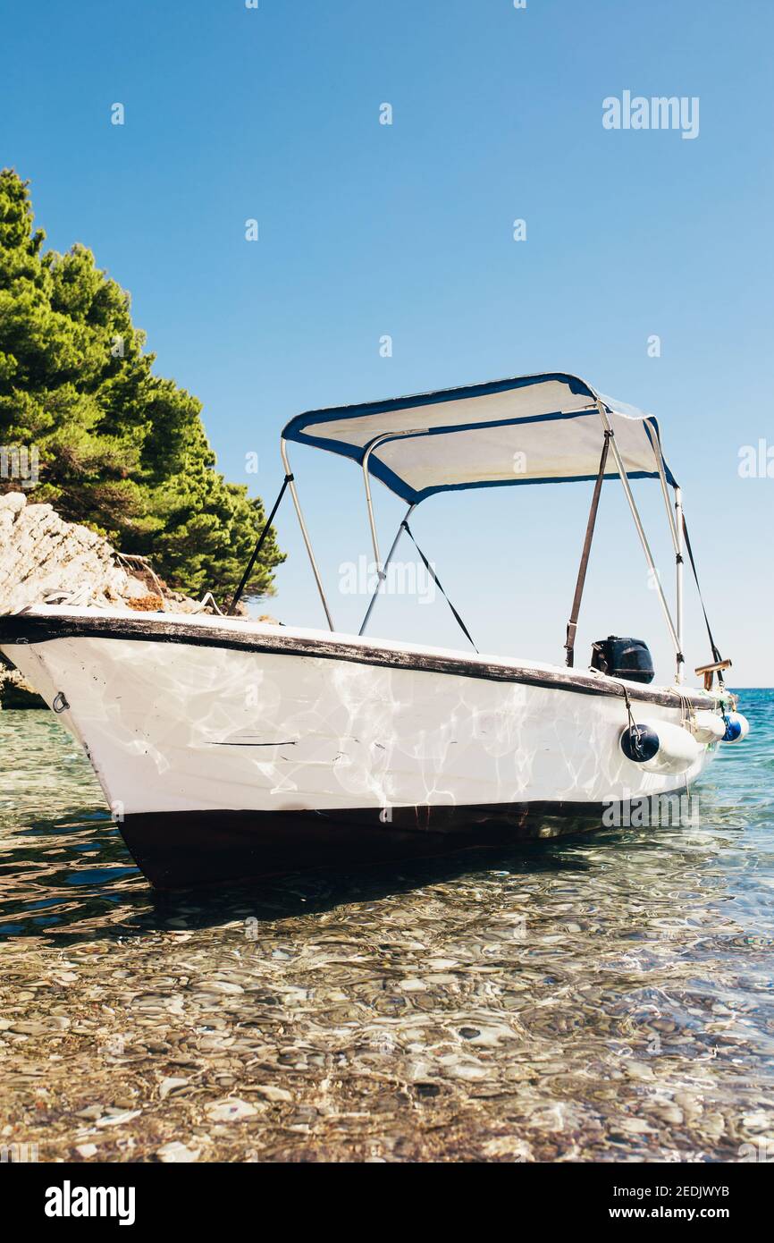 White boat with a canopy on the waves near the shore - transparent sea ...