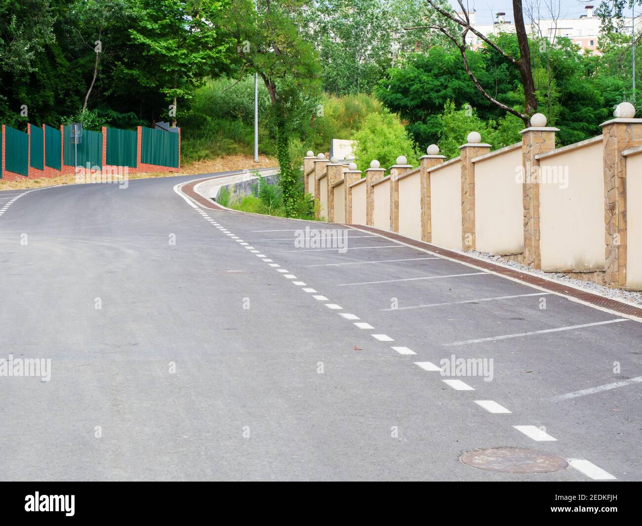 A road leading upward with fence on both sides and green trees along ...