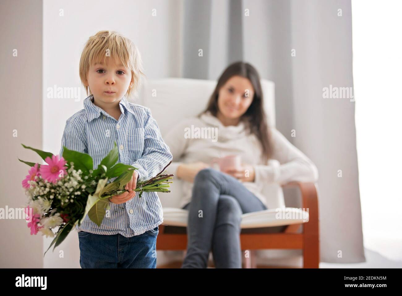 Beautiful blond boy, giving mother flowers and box with little gift for ...