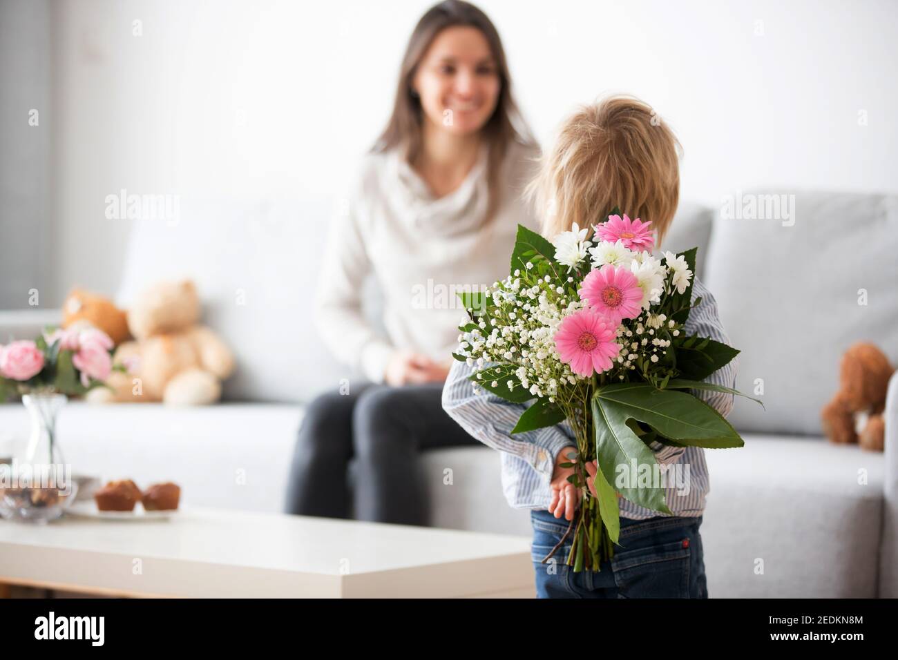 Beautiful blond boy, giving mother flowers and box with little gift for ...