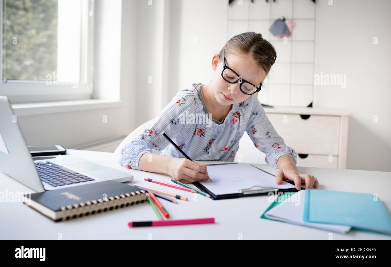 Pretty teenager girl doing homework sitting behind the table at home ...