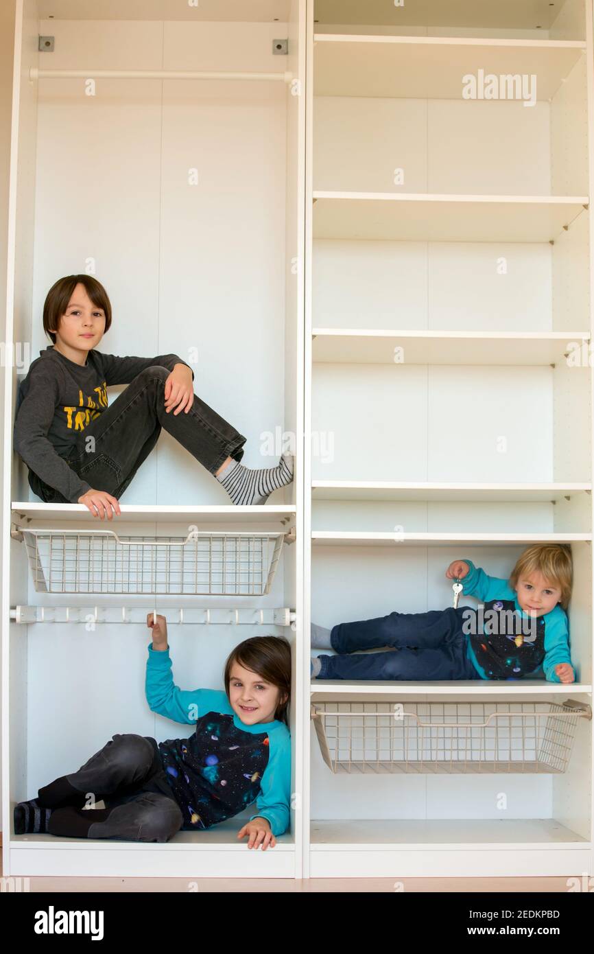 Cute child, sit in a white box in open wardrope, making funny faces ...