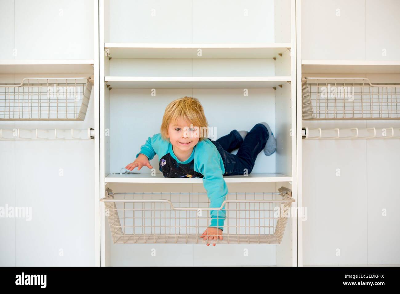 Cute child, sit in a white box in open wardrope, making funny faces ...