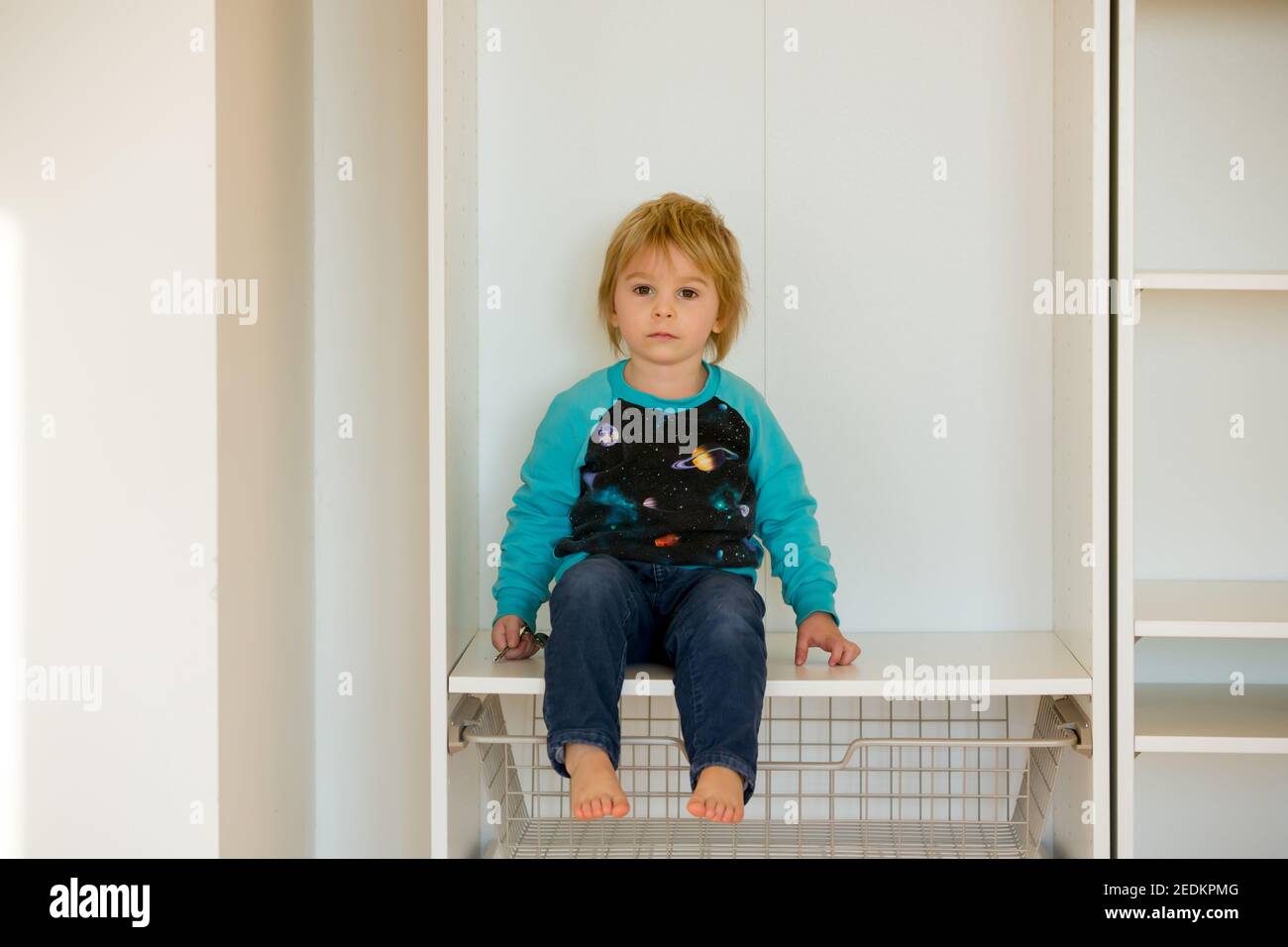 Cute child, sit in a white box in open wardrope, making funny faces ...