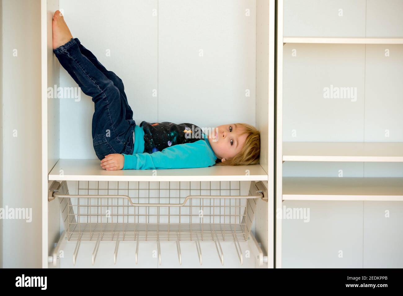 Cute child, sit in a white box in open wardrope, making funny faces ...