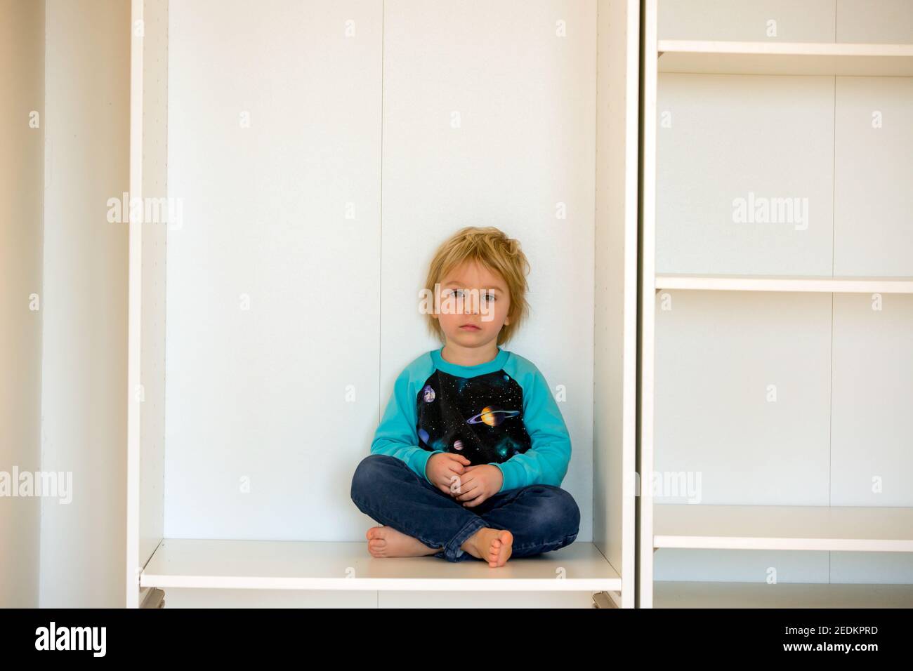 Cute child, sit in a white box in open wardrope, making funny faces ...