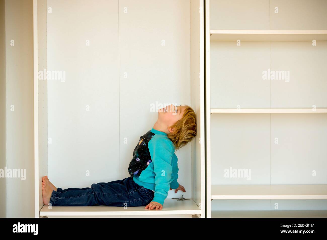 Cute child, sit in a white box in open wardrope, making funny faces ...