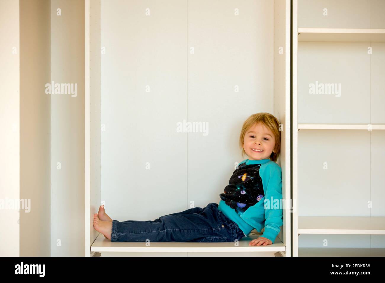 Cute child, sit in a white box in open wardrope, making funny faces ...