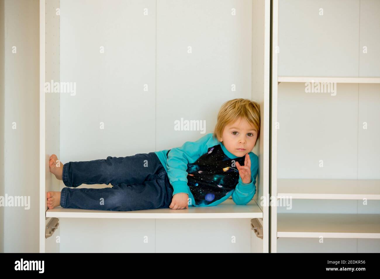 Cute child, sit in a white box in open wardrope, making funny faces ...