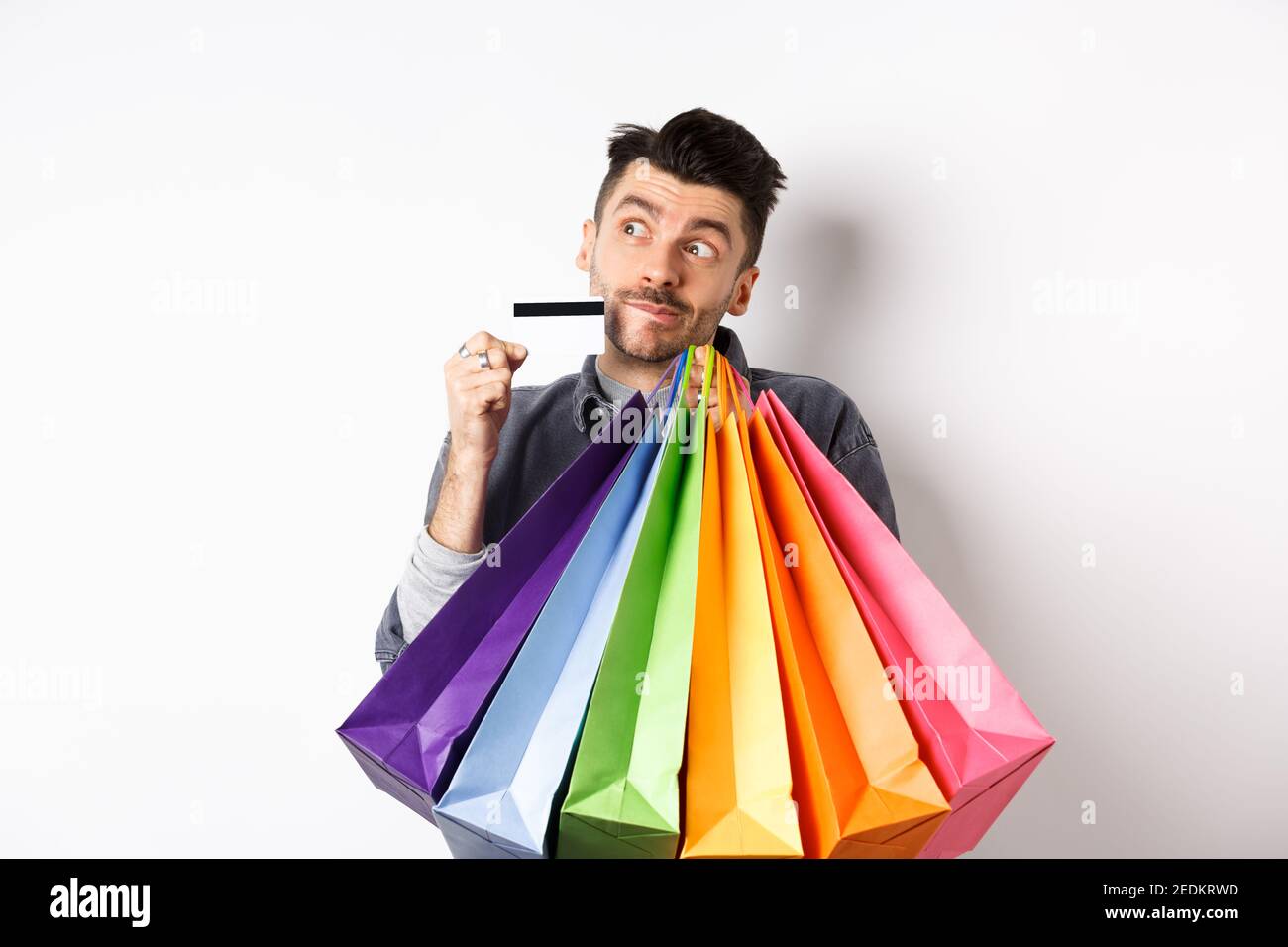 Dreamy guy thinking of shopping, holding colorful bags with purchased ...