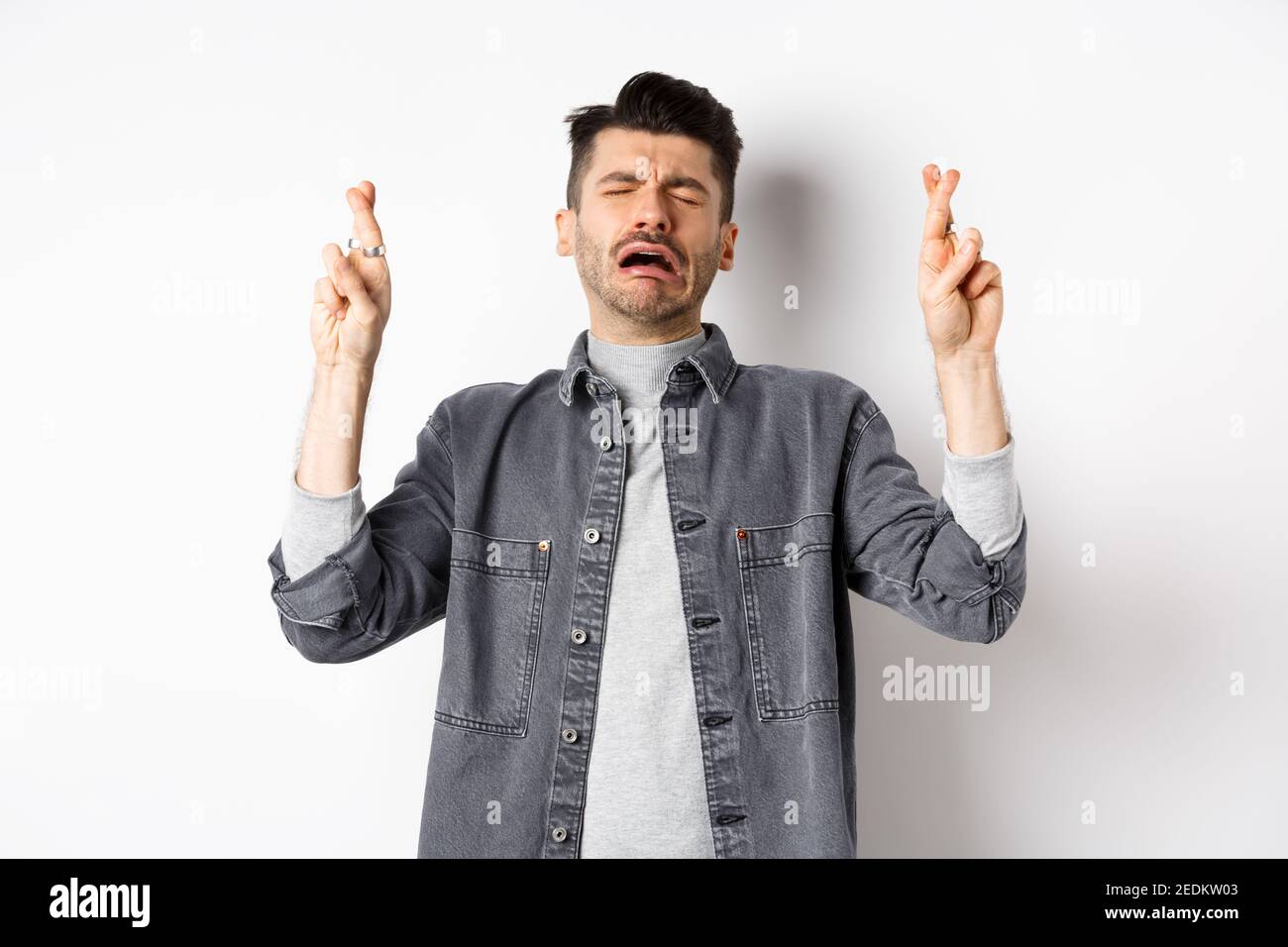 Sad and miserable man hoping god, cross fingers and crying, praying or ...