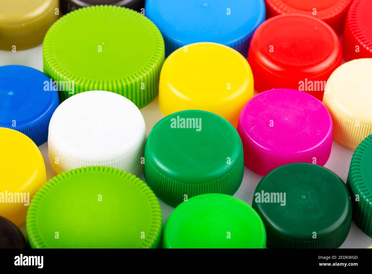 Many multi-colored plastic bottle caps on a white background. Recycling ...