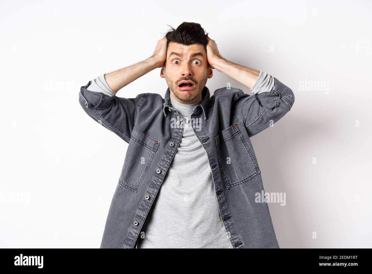 Alarmed young man grab head and pop eyes at camera, looking worried and ...