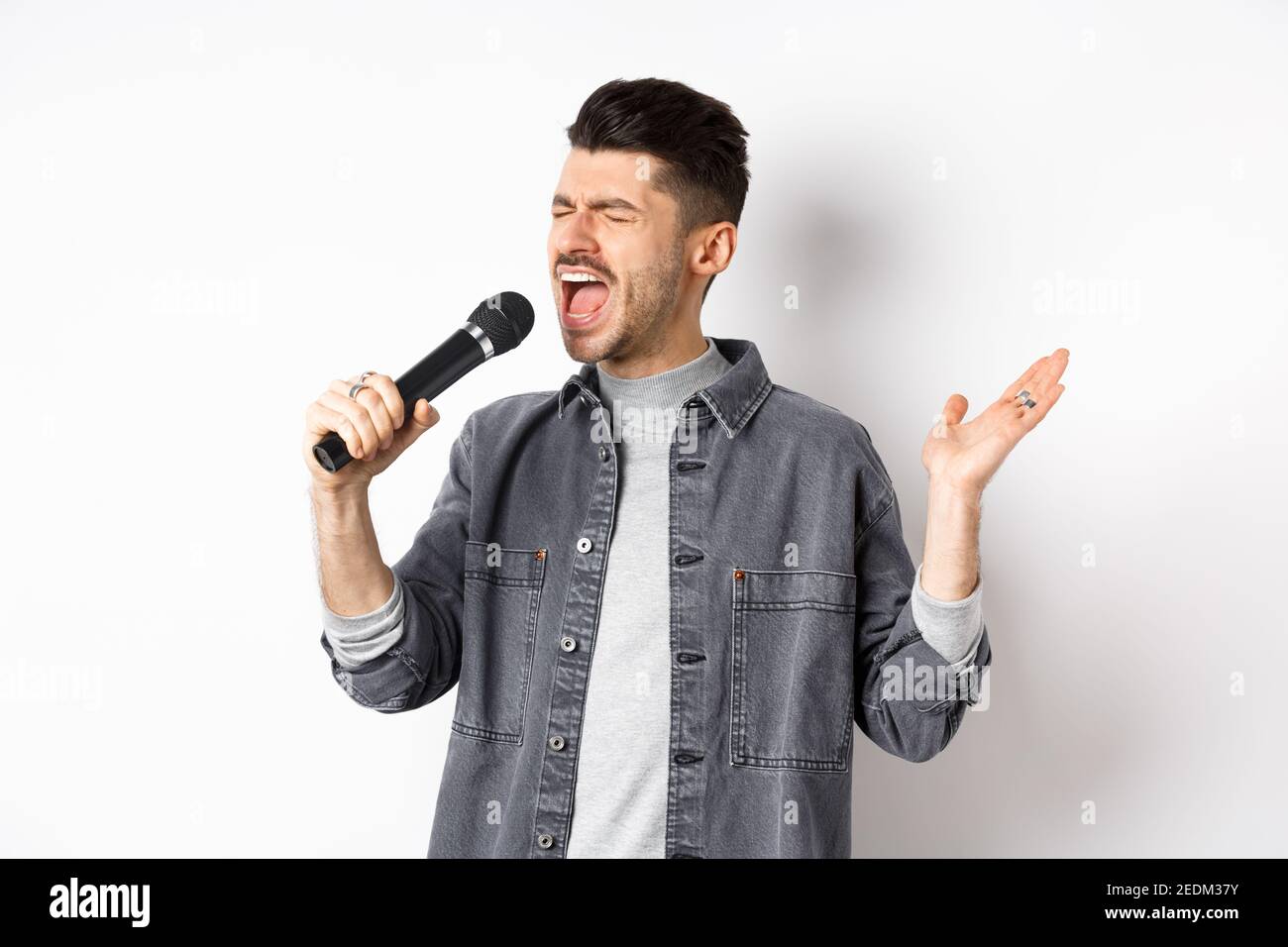 Handsome guy singing in mic with passion, perform for audience, holding ...