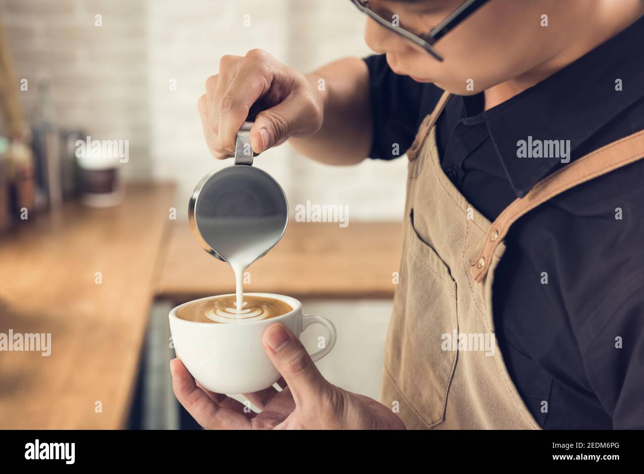 Professional barista pouring steamed milk into coffee cup making ...