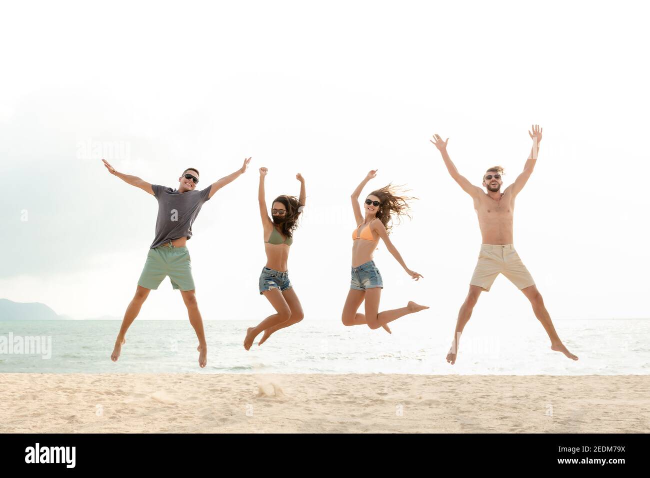 Happy young energetic group of friends jumping at the beach on summer ...