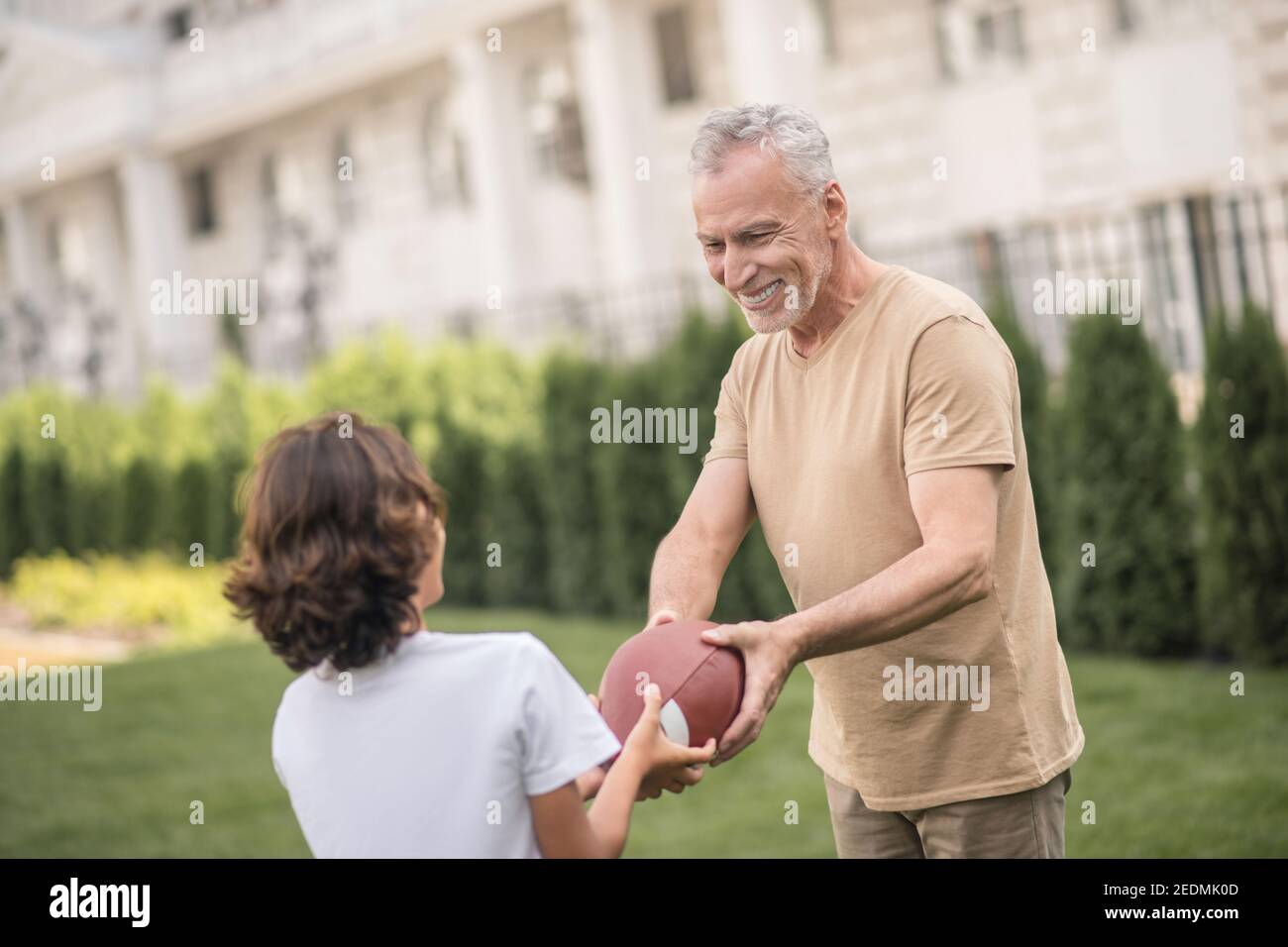 Gray-haired dad giving a ball to his son and smiling Stock Photo - Alamy