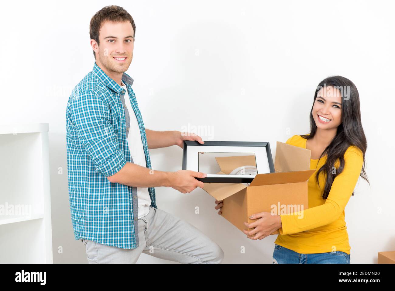 Happy young interracial couple helping eaching other moving into new ...