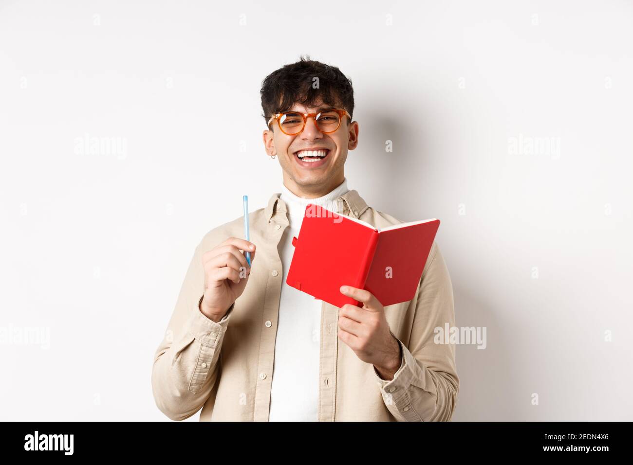 Cheerful young man in glasses laughing and taking notes, writing down ...