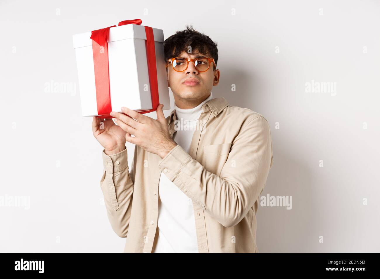 Intrigued guy listening whats inside gift box, trying guess present ...