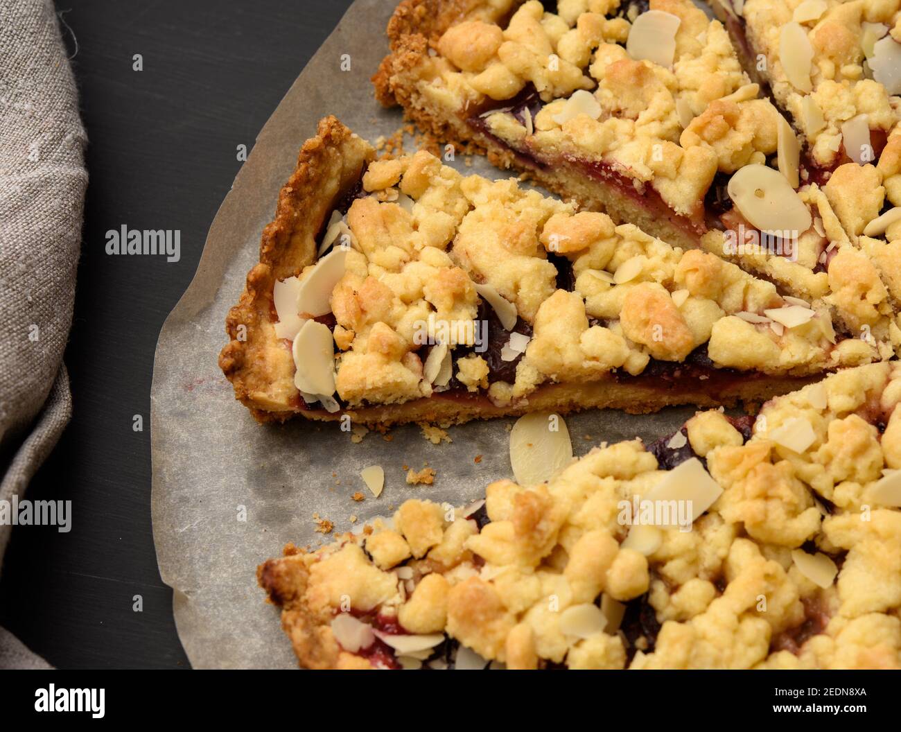 baked round crumble pie with plum cut into pieces on a black background ...