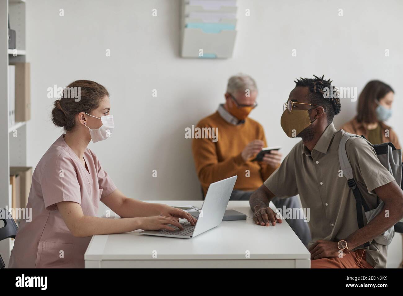Side view portrait of female nurse registering patients waiting in row ...