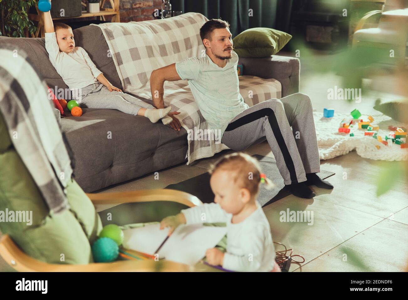 Squats with sofa. Young man exercising fitness, aerobic, yoga at home ...