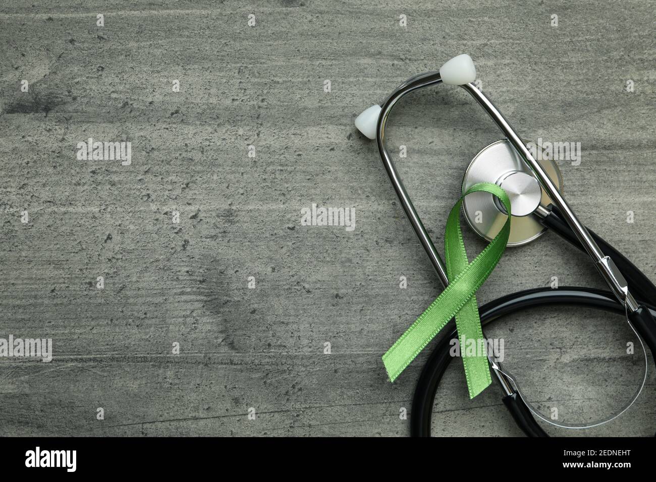 Green awareness ribbon and stethoscope on gray textured background ...