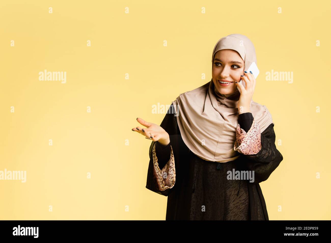 Phone talking. Beautiful young arab woman in stylish hijab on yellow ...